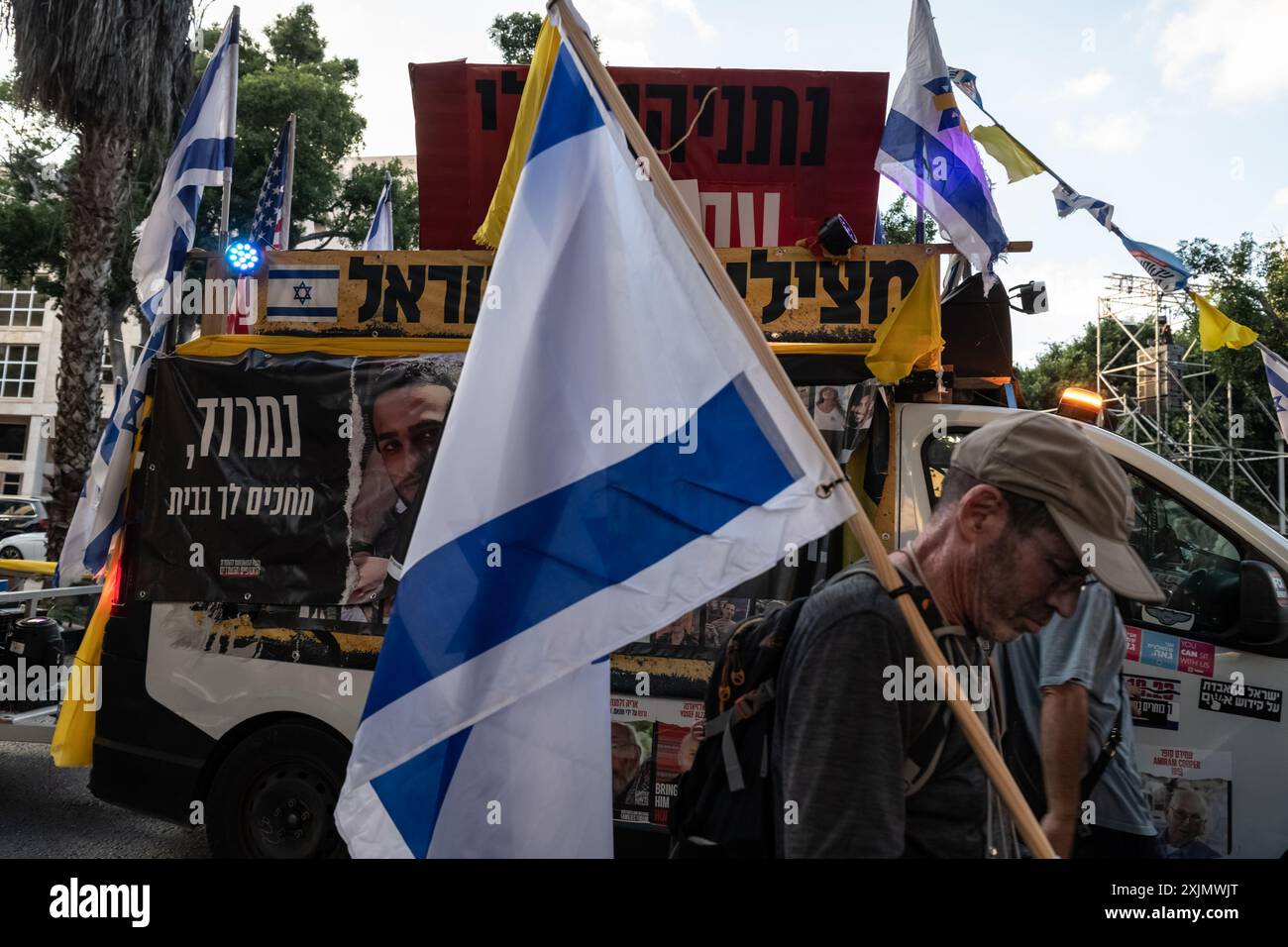 A man with an Israeli flag is passing in front of a van with speakers ...