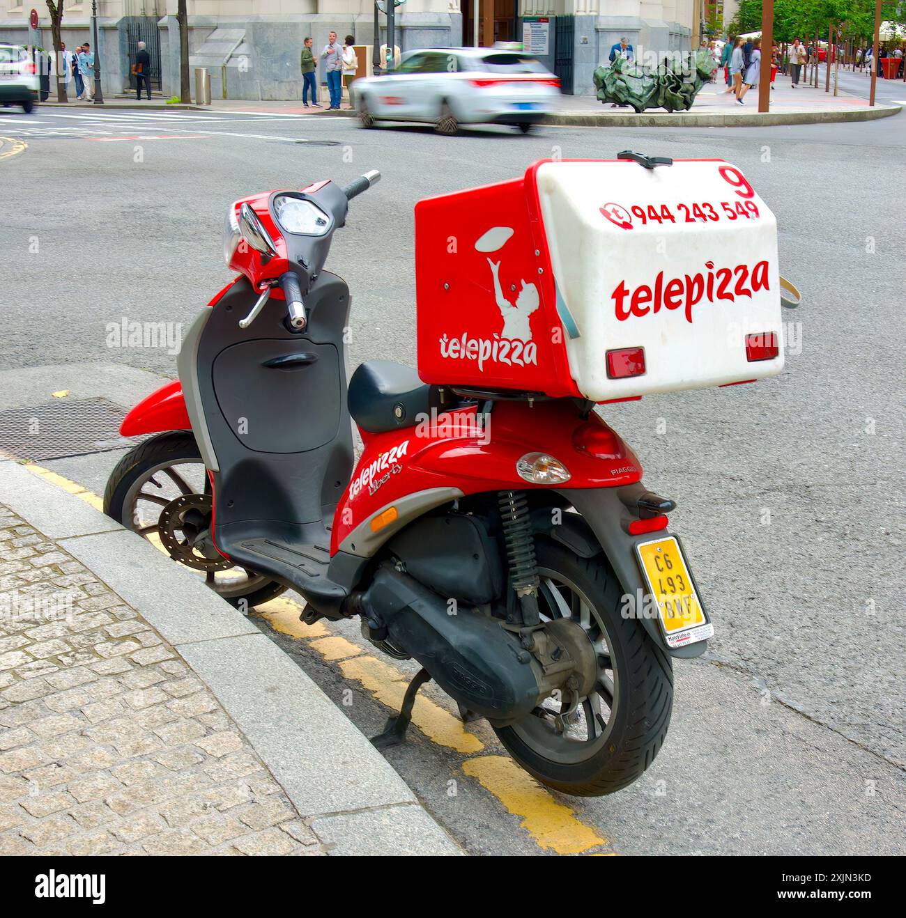 A delivery drivers red and white Telepizza moped parked on a yellow ...