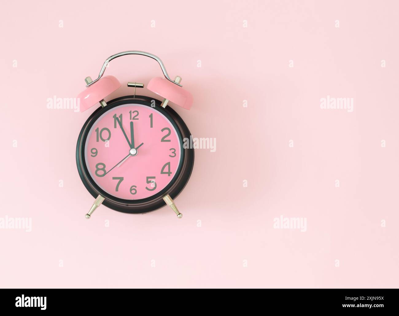 Pastel pink and black alarm clock on light pastel pink background with ...