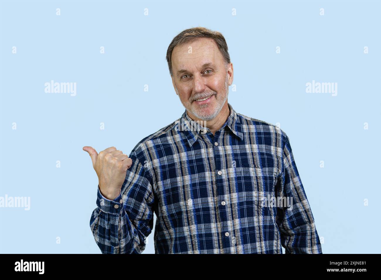 Portrait of smiling mature man pointing back with his thumb up ...