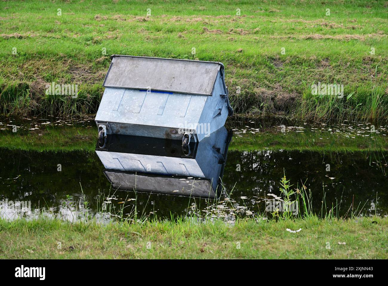 Metal industrial bin floating in a ditch Stock Photo - Alamy