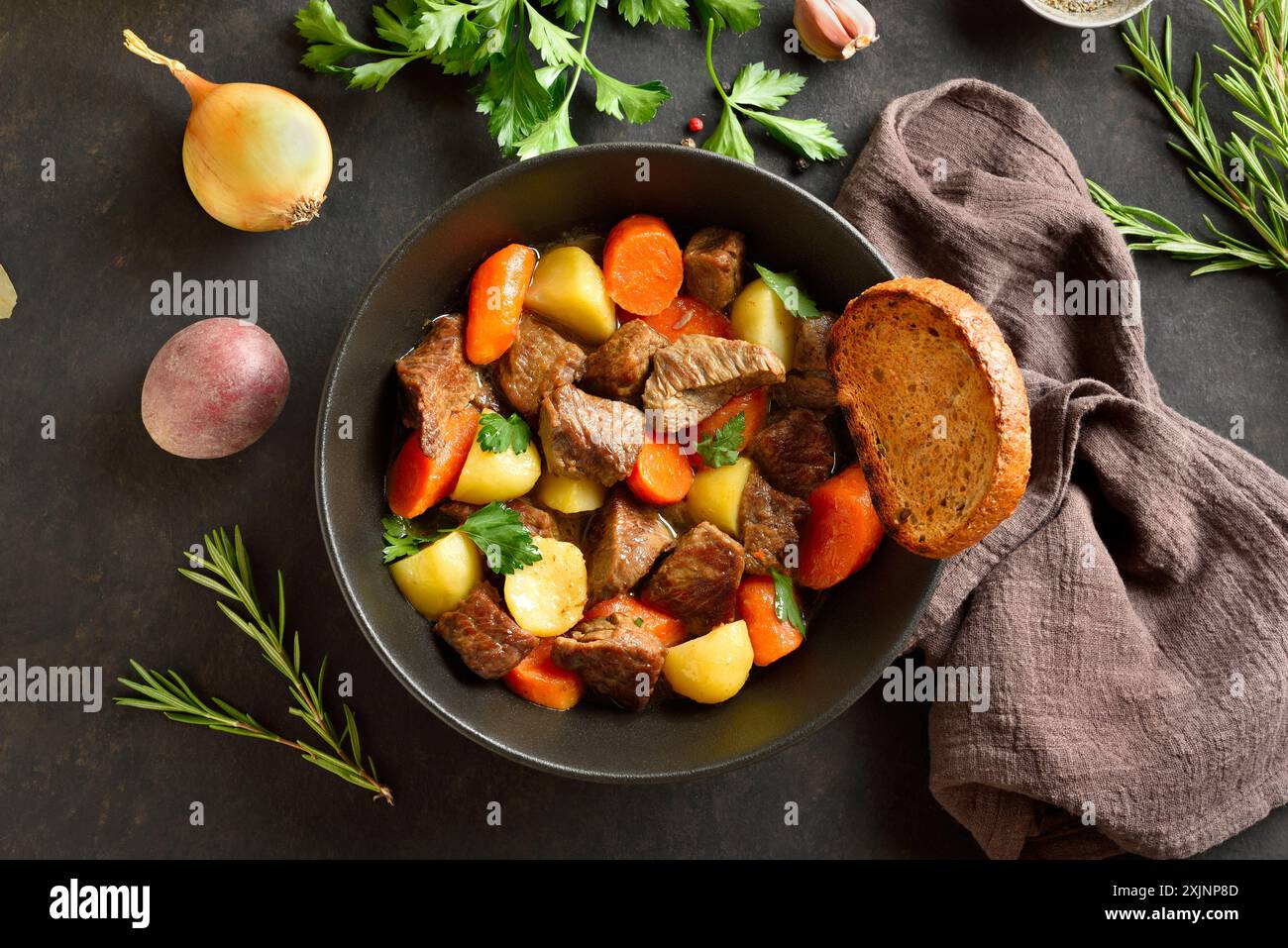 Beef stew with potatoes, carrots and greens in bowl over dark stone ...