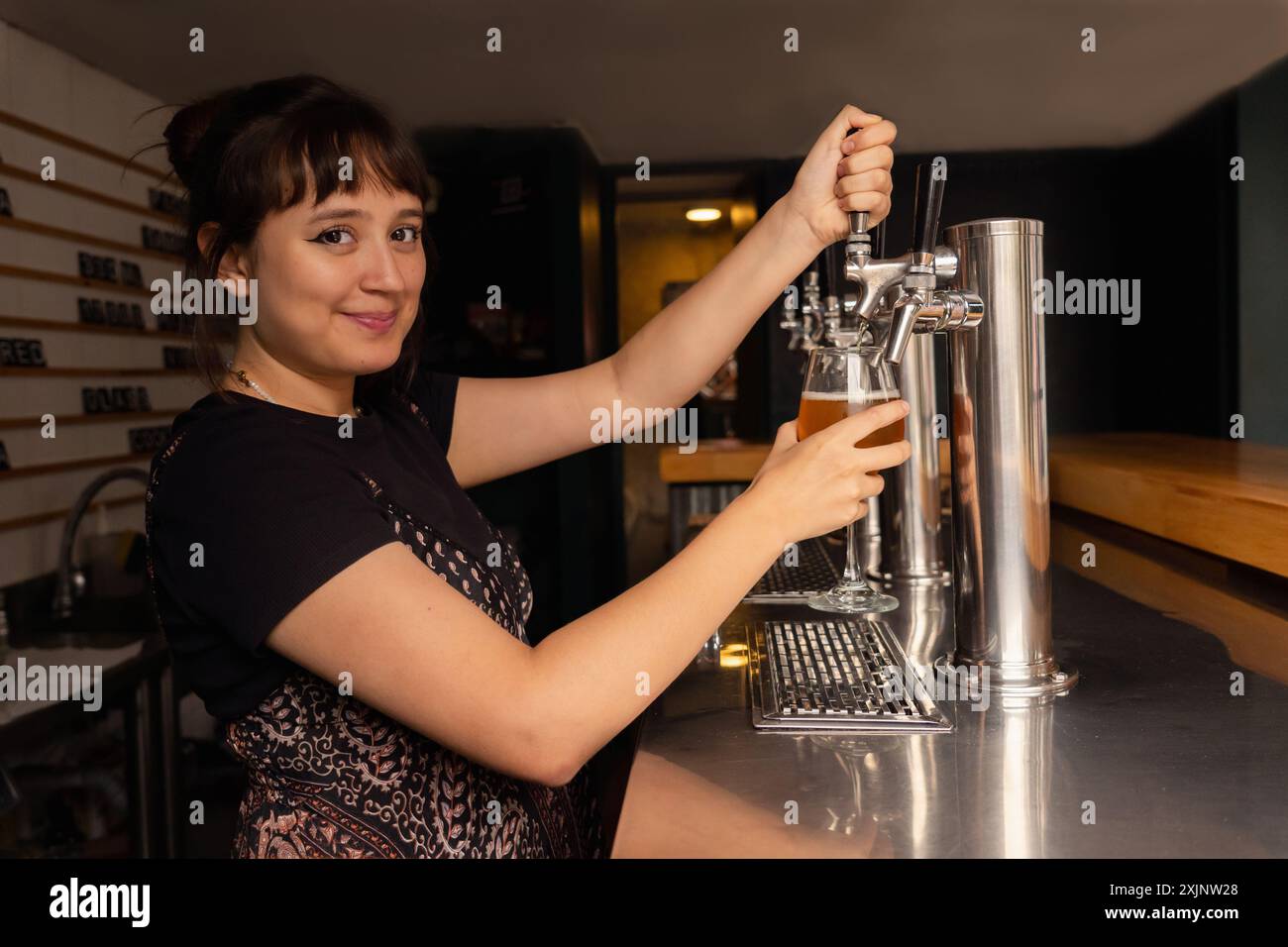 Portrait of waitress in profile filling a glass of beer from the tap ...