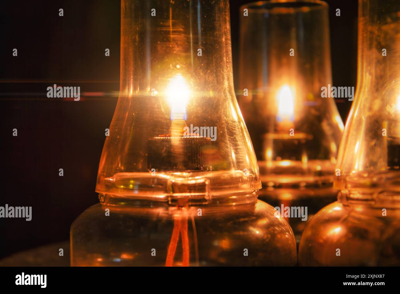 three glass paraffin kerosene lamp lit on a table, orange glow, flame ...