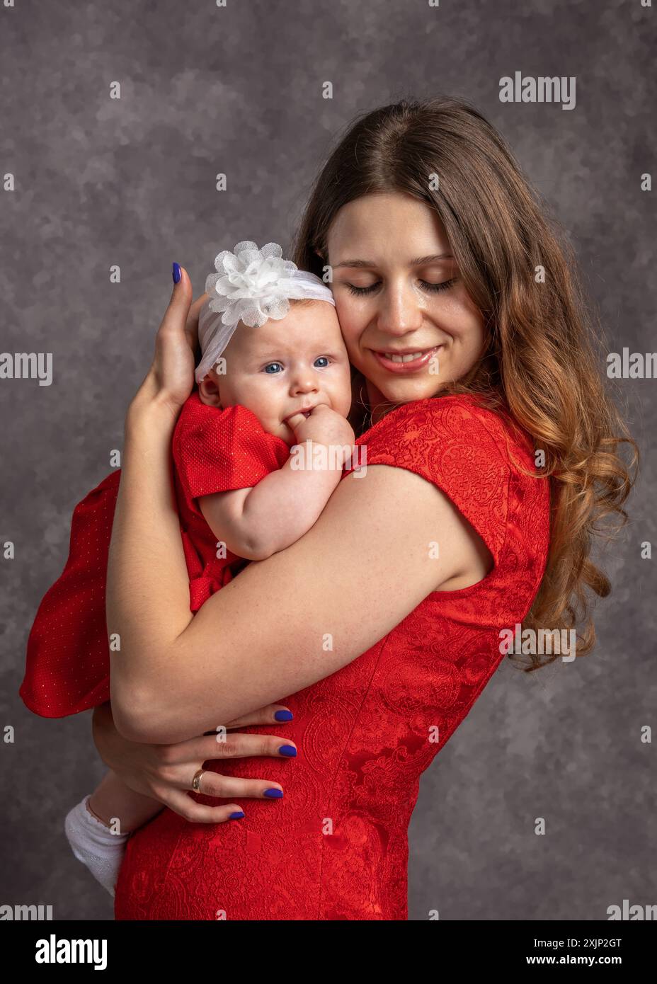 Mom gently hugs her little daughter. Dressed in red dresses. Gray ...