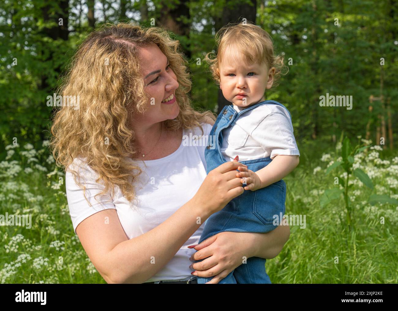 A happy mother with wavy hair holds and hugs a little blond boy with ...