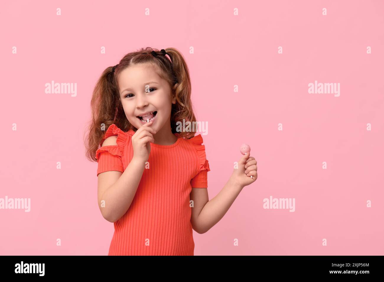 Cute little girl licking lollipop on pink background Stock Photo - Alamy