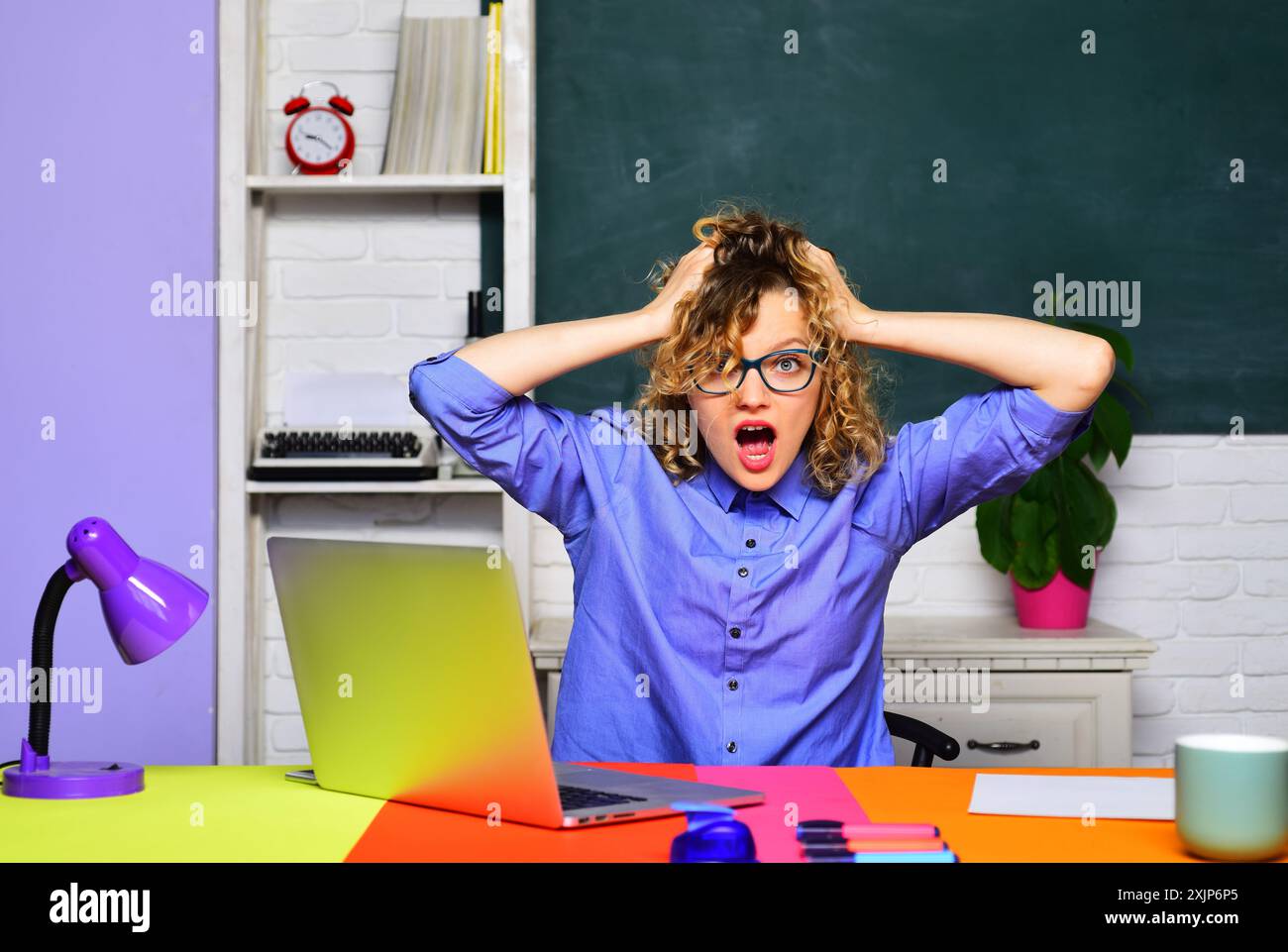 Shocked frustrated female teacher with hands on head sitting at desk ...