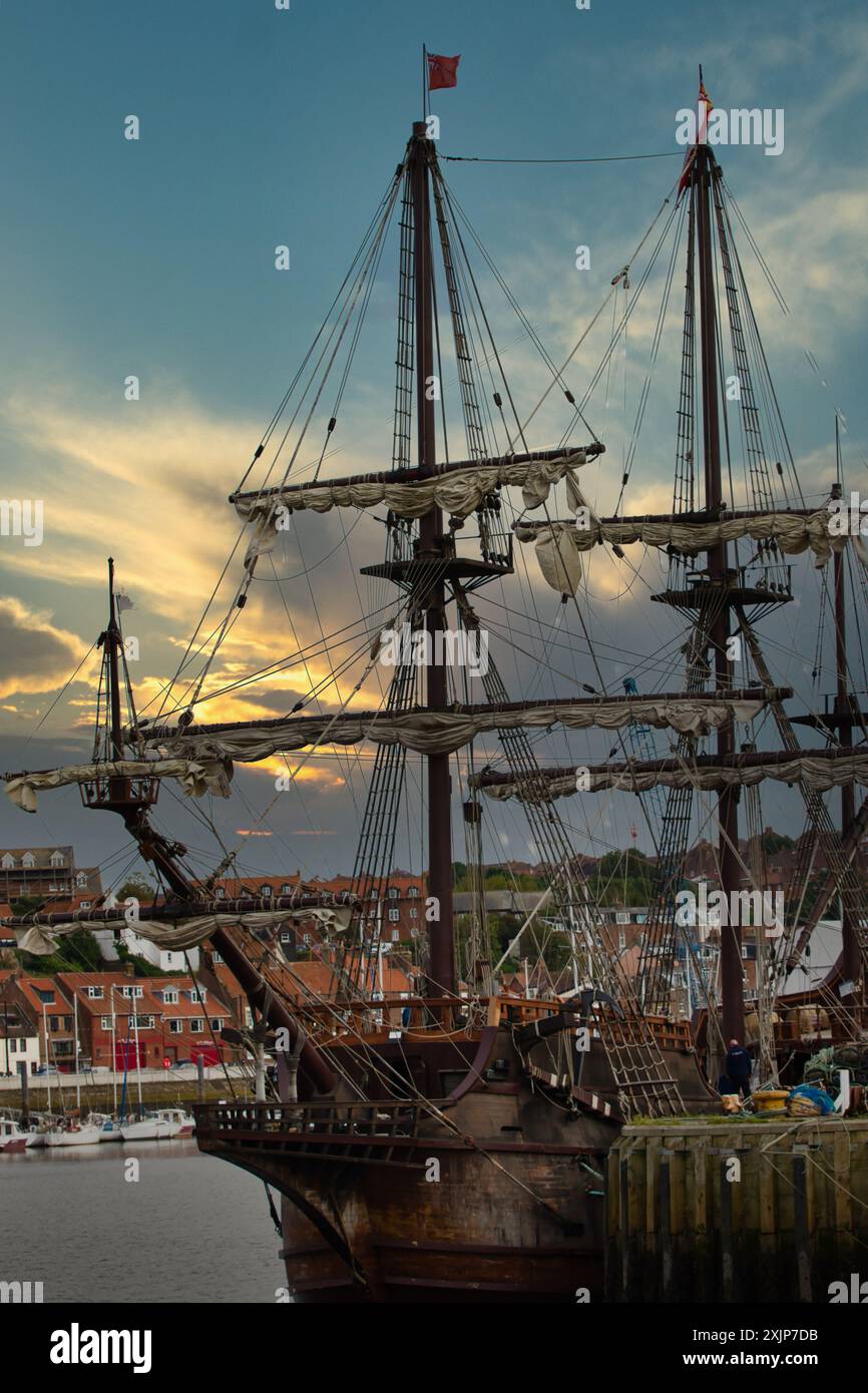 A historic sailing ship docked at a harbor with a sunset in the ...