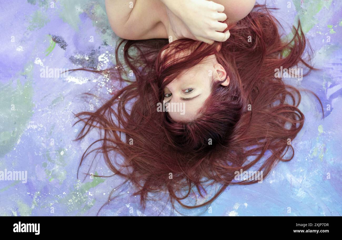 Woman with long red hair lies on a colorful, abstract background, her ...