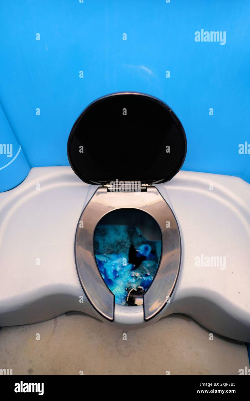 Open toilet in portable bathroom with focus on seat and blurred blue ...