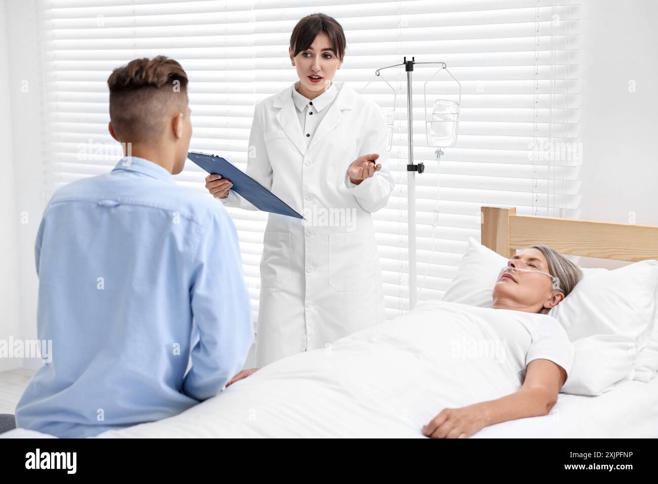 Coma patient. Sad young man near his unconscious mother talking with ...