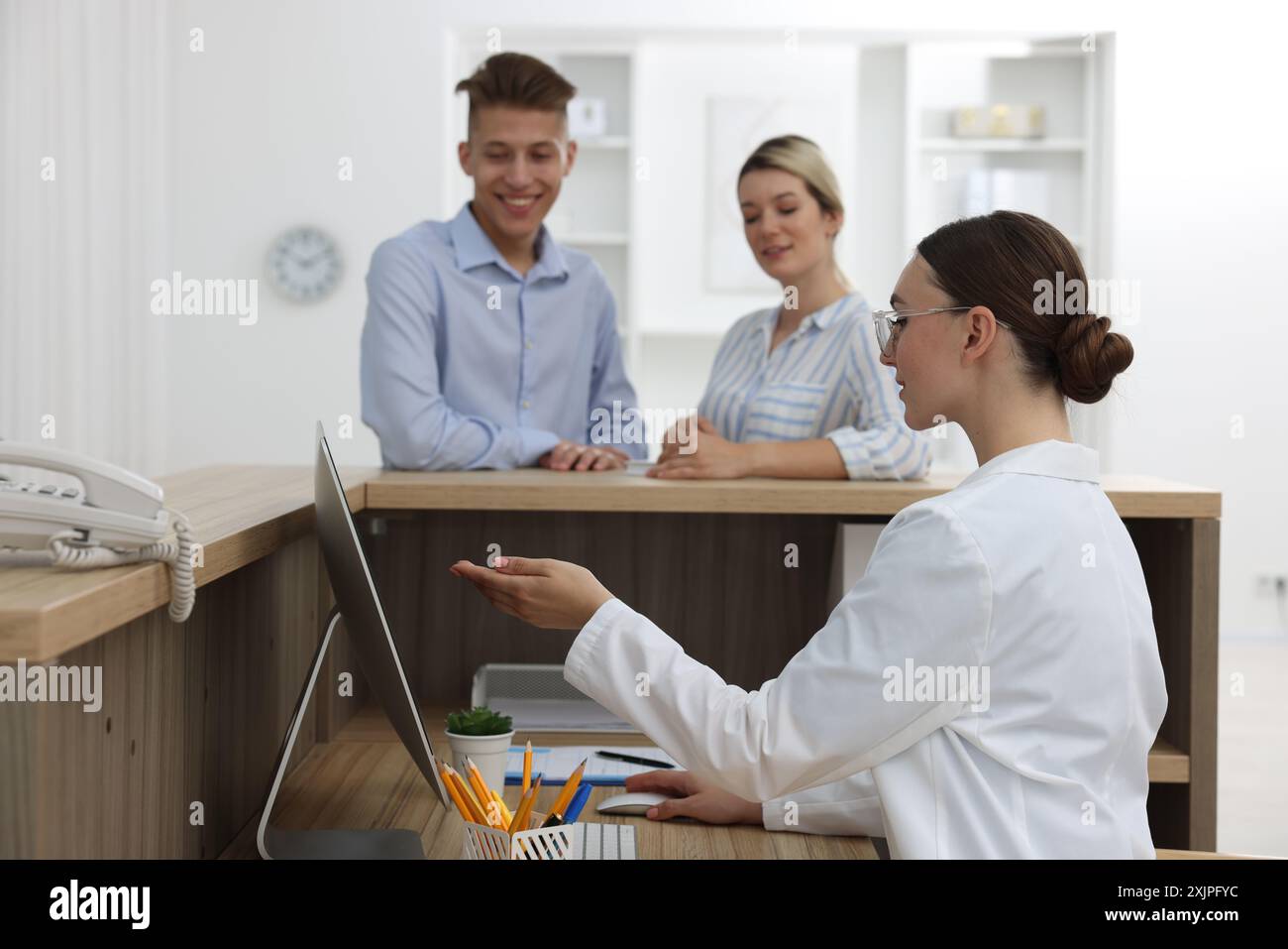 Professional receptionist working with patients at wooden desk in ...