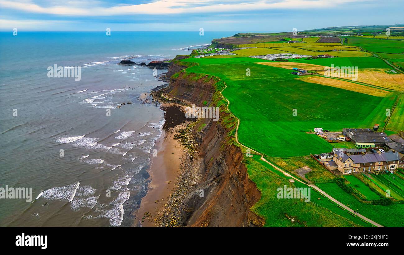 Aerial view of a coastal cliff with green fields and houses on top ...