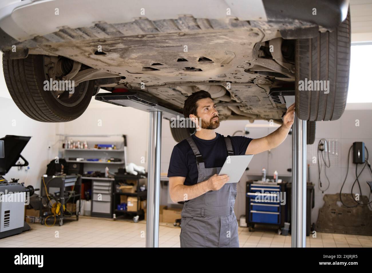 Mechanic inspecting car on lift in auto repair shop Stock Photo - Alamy