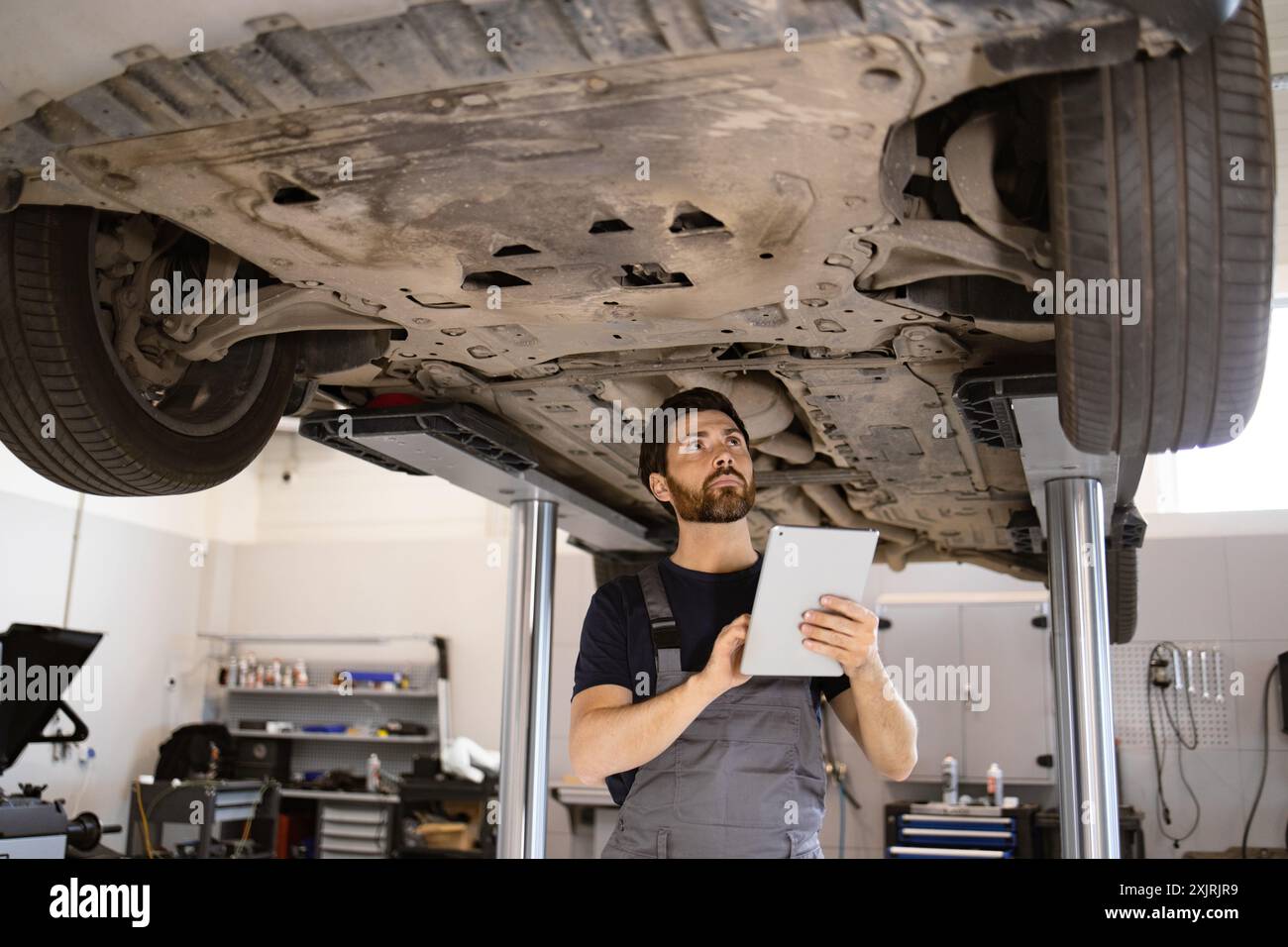 Mechanic inspecting undercarriage of car in auto repair shop Stock Photo - Alamy