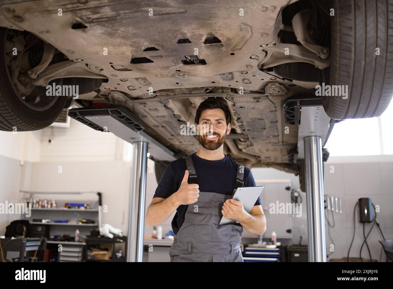 Mechanic under car lift giving thumbs up in garage Stock Photo - Alamy