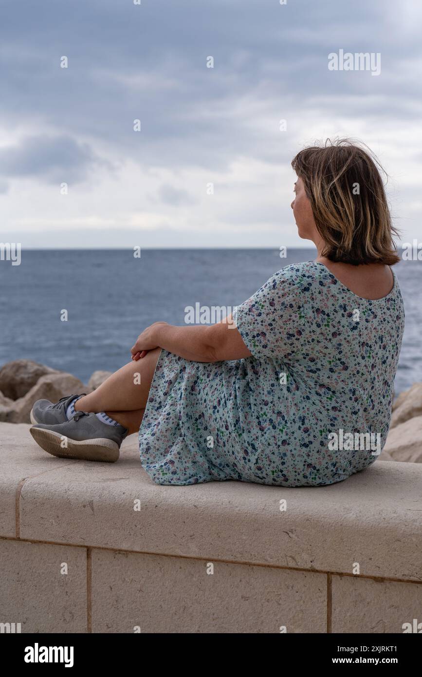 A middle-aged woman sits on the beach and looks into the distance ...