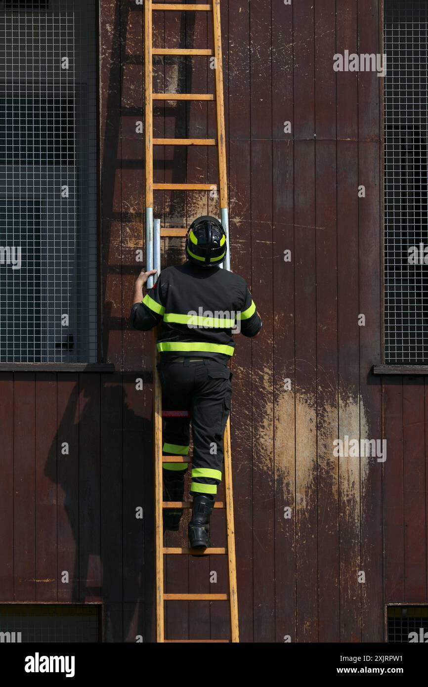 Firefighter in uniform with portective helmet climbing ladder during ...