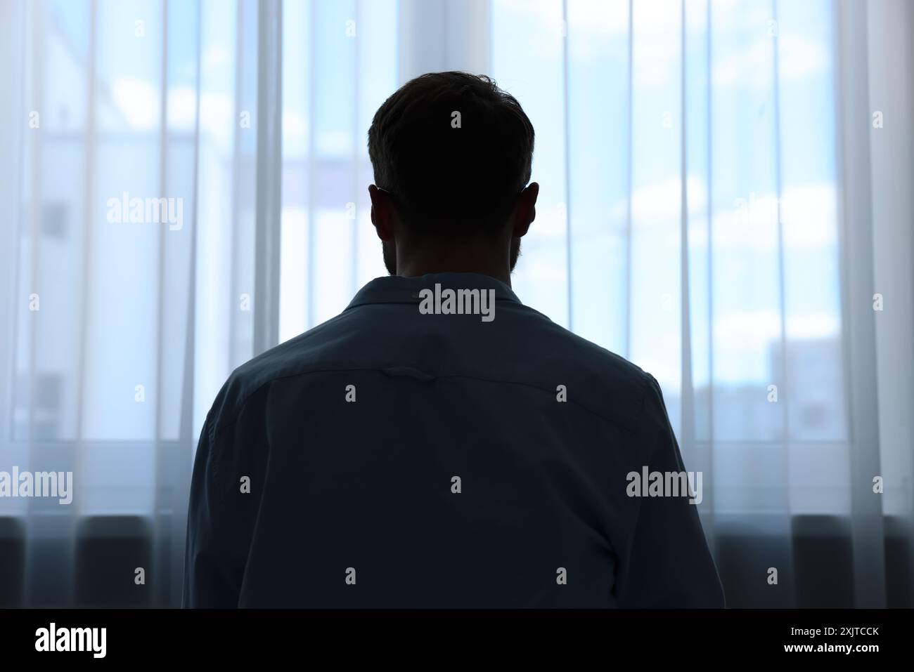 Loneliness concept. Sad man near window at home, back view Stock Photo ...