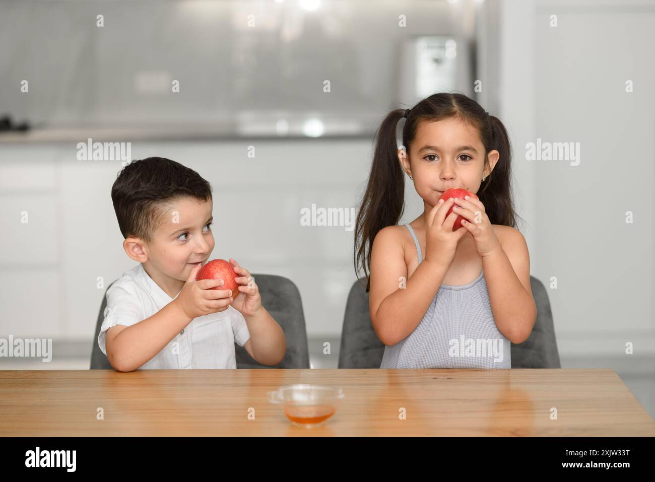 In the kitchen, adorable siblings enjoy fresh apples together, creating ...