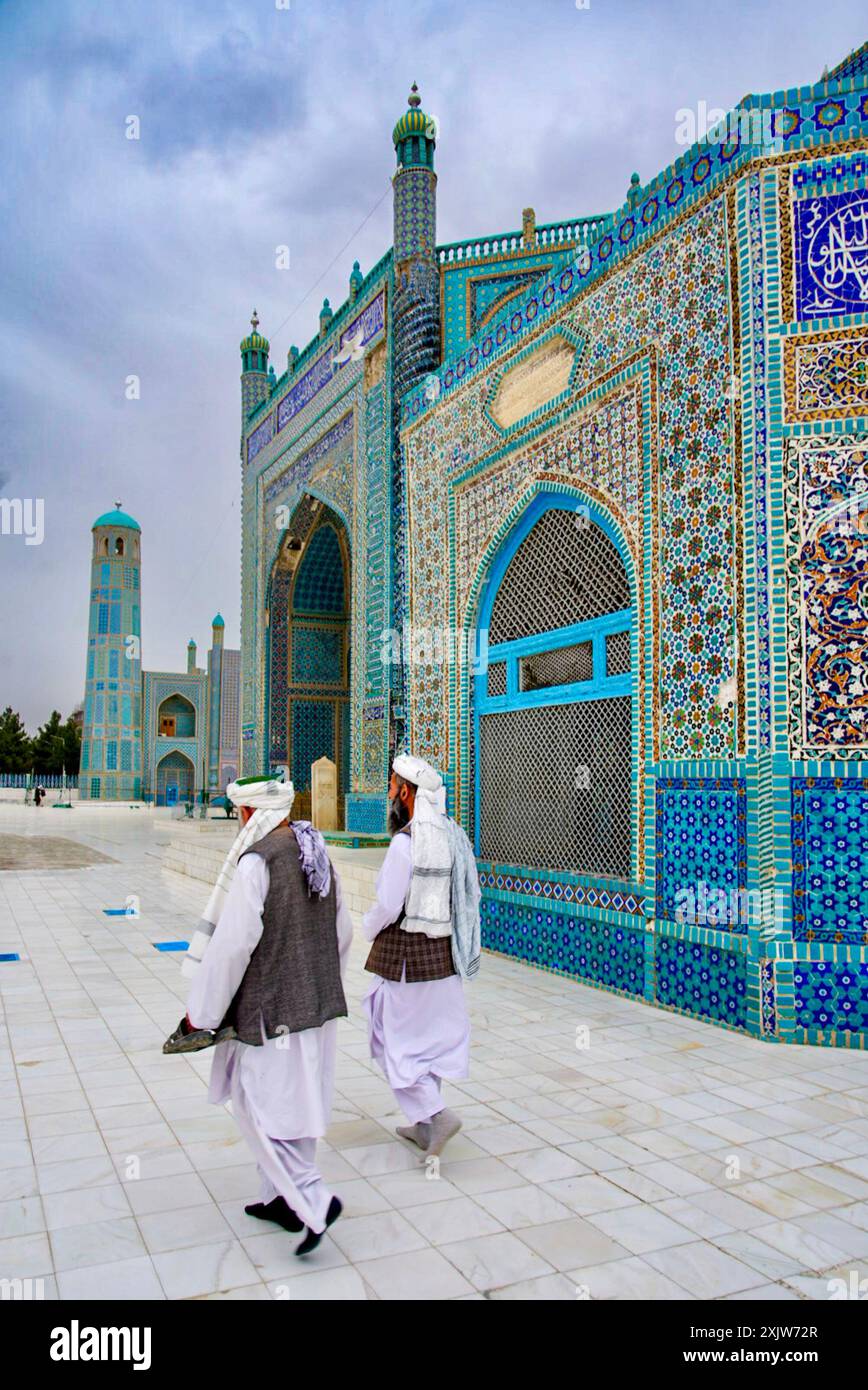 Two Afghan men in traditional attire walk past the Shrine of Hazrat Ali ...