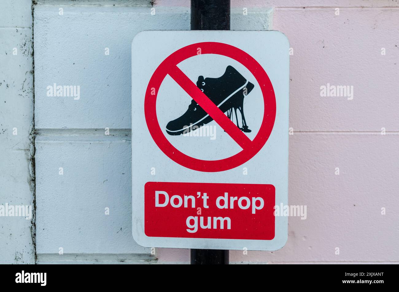 A 'Don't Drop Gum' sign on a black metal post with a wall as background ...