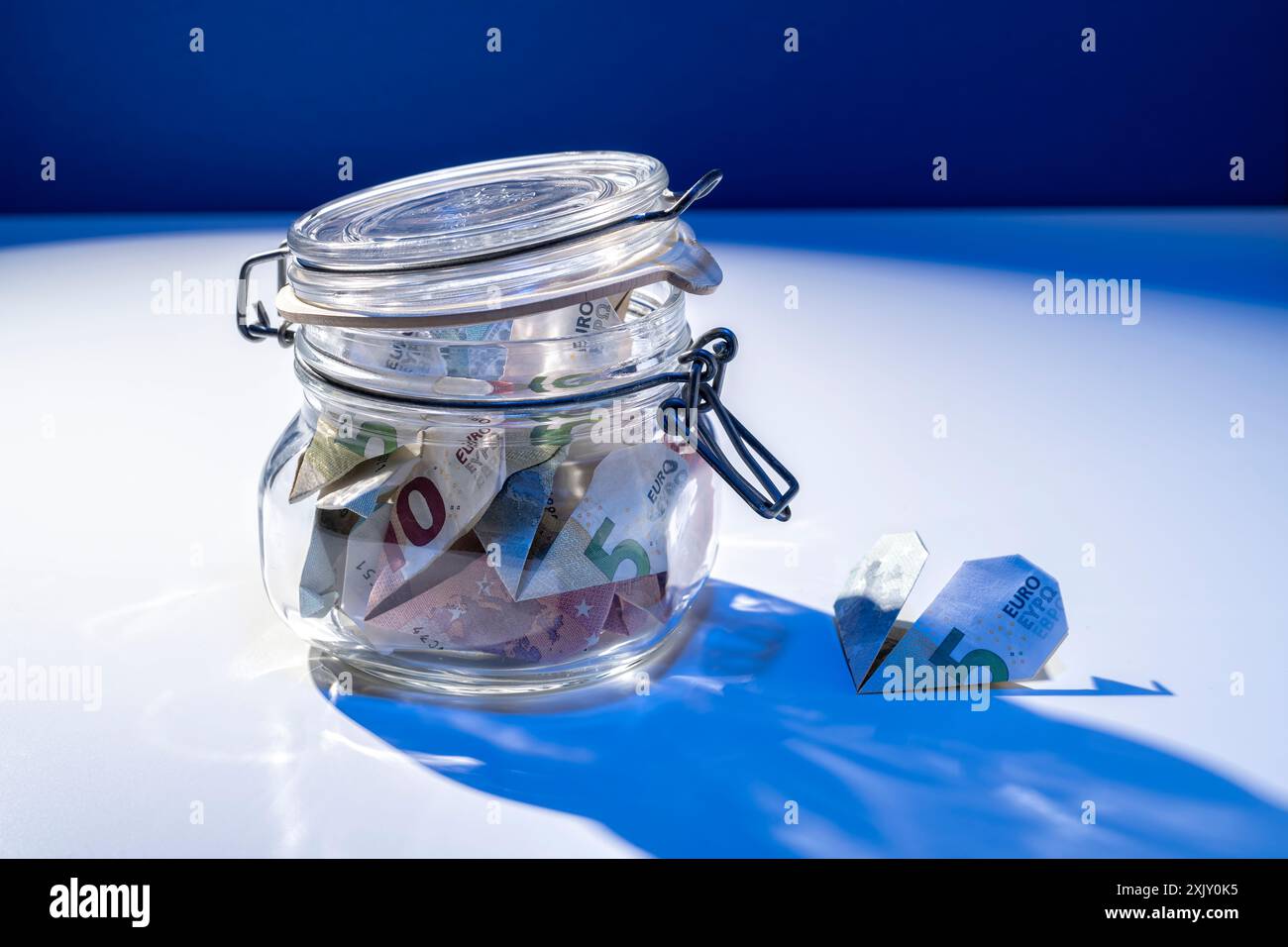 Folded banknotes as savings in an open jar with a hard blue shadow ...