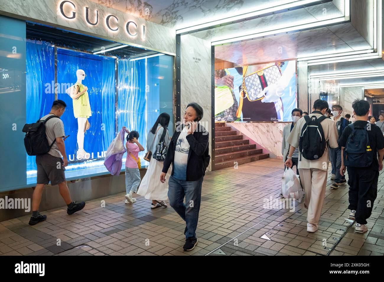 Shoppers walk past the Italian luxury fashion brand Gucci logo and ...