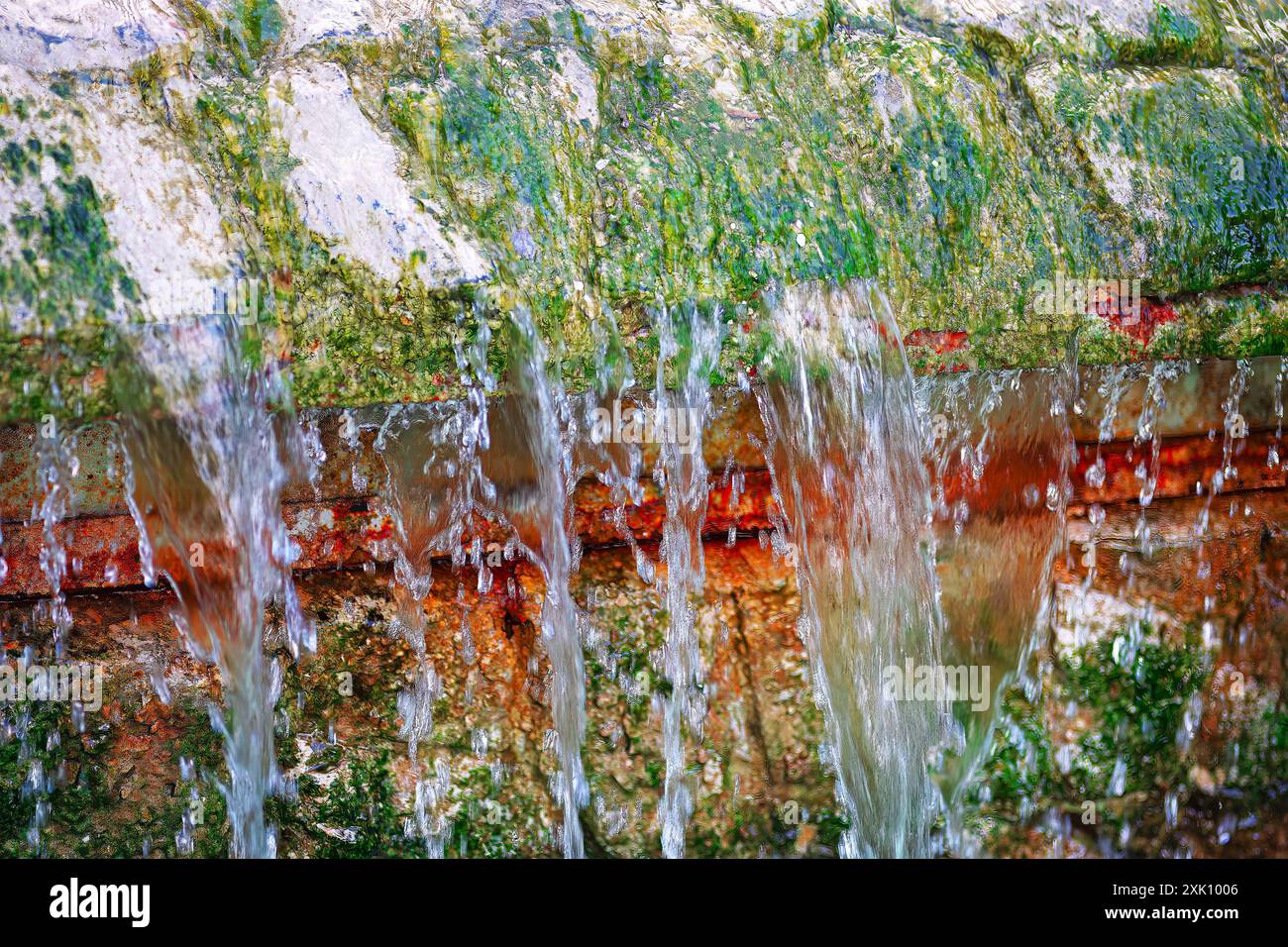 Stone wall with water dripping from it. The water is green and brown ...