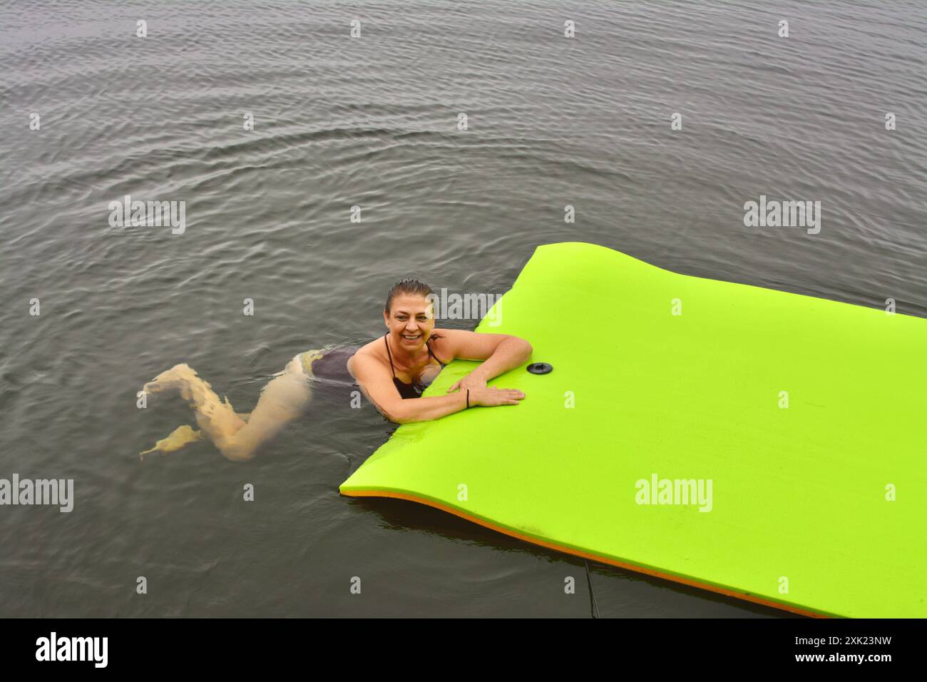 55 year old woman in a bathing suit swimming in a lake holding onto a ...