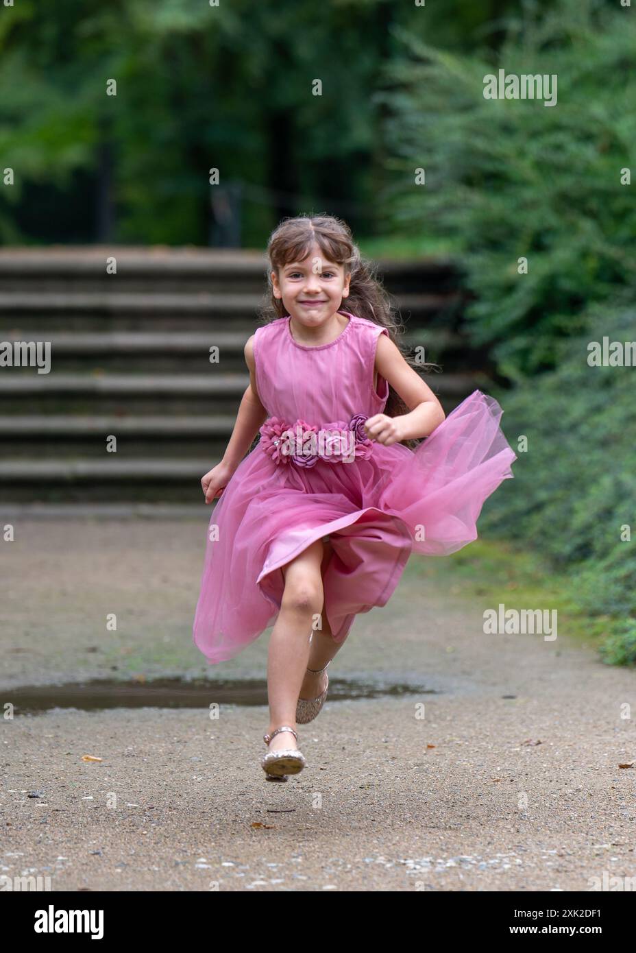 A little cute girl in a beautiful pink dress with long hair runs ...