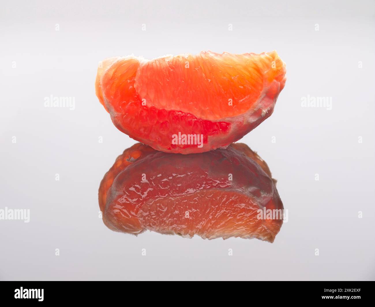 A close up studio photo of a slice of grapefruit set on a reflective ...
