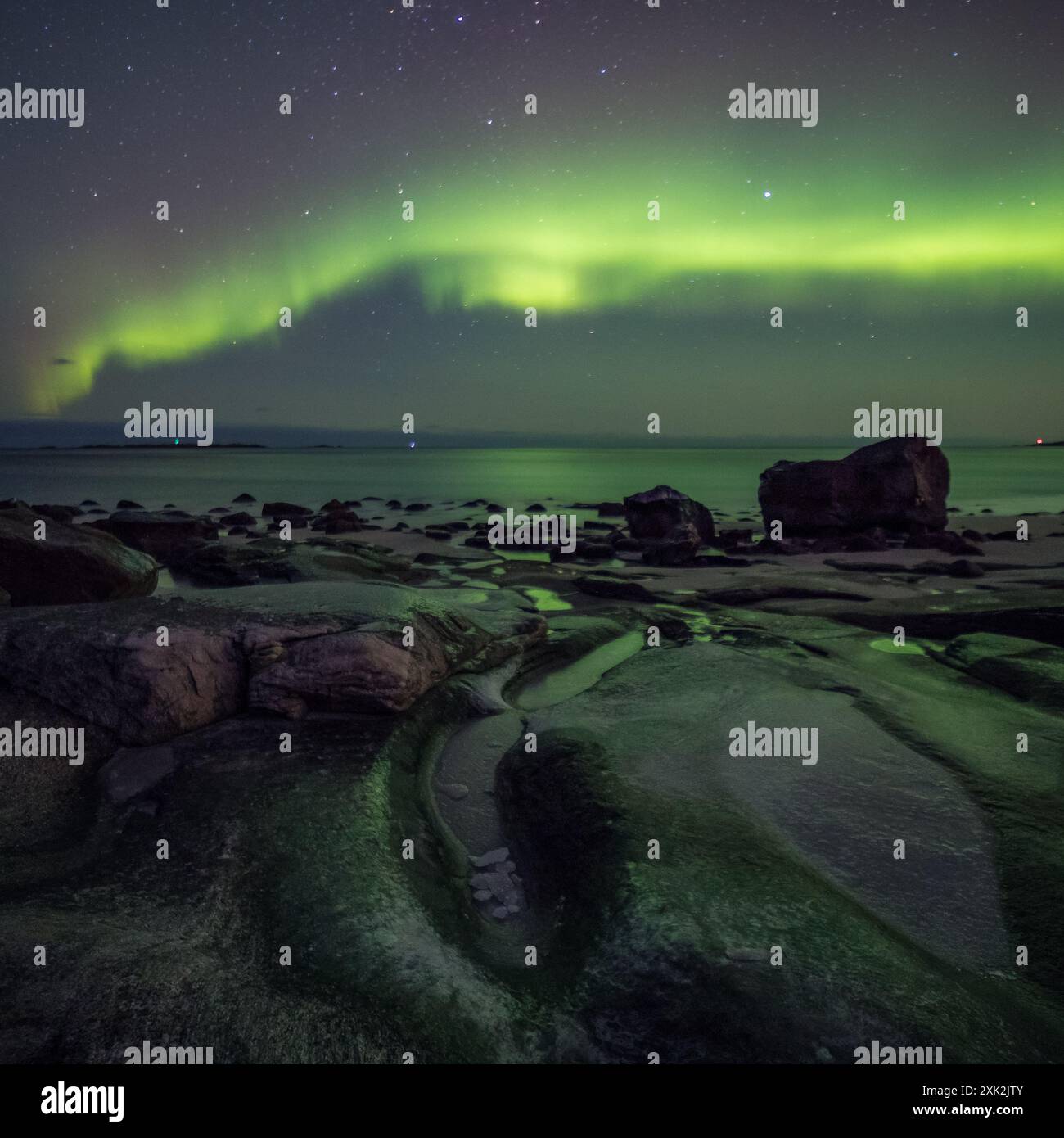 Spectacular view of aurora borealis dancing over a mossy, rocky beach ...