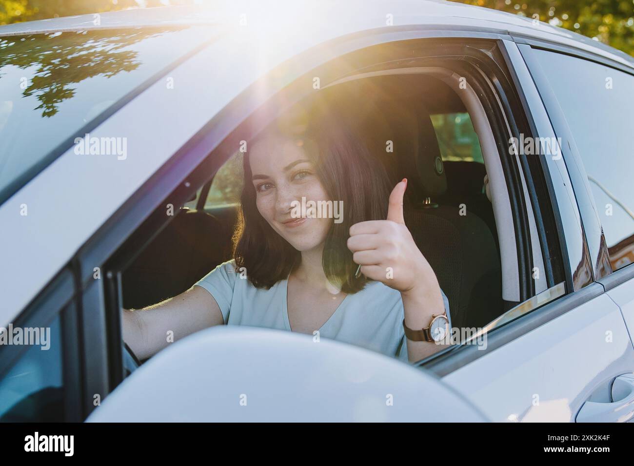 A youthful female driver smiles while giving a thumbs-up gesture from ...