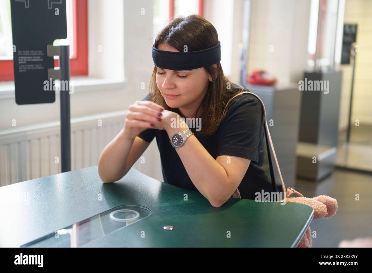 A young woman sits at a table with a sensor headband that measures ...