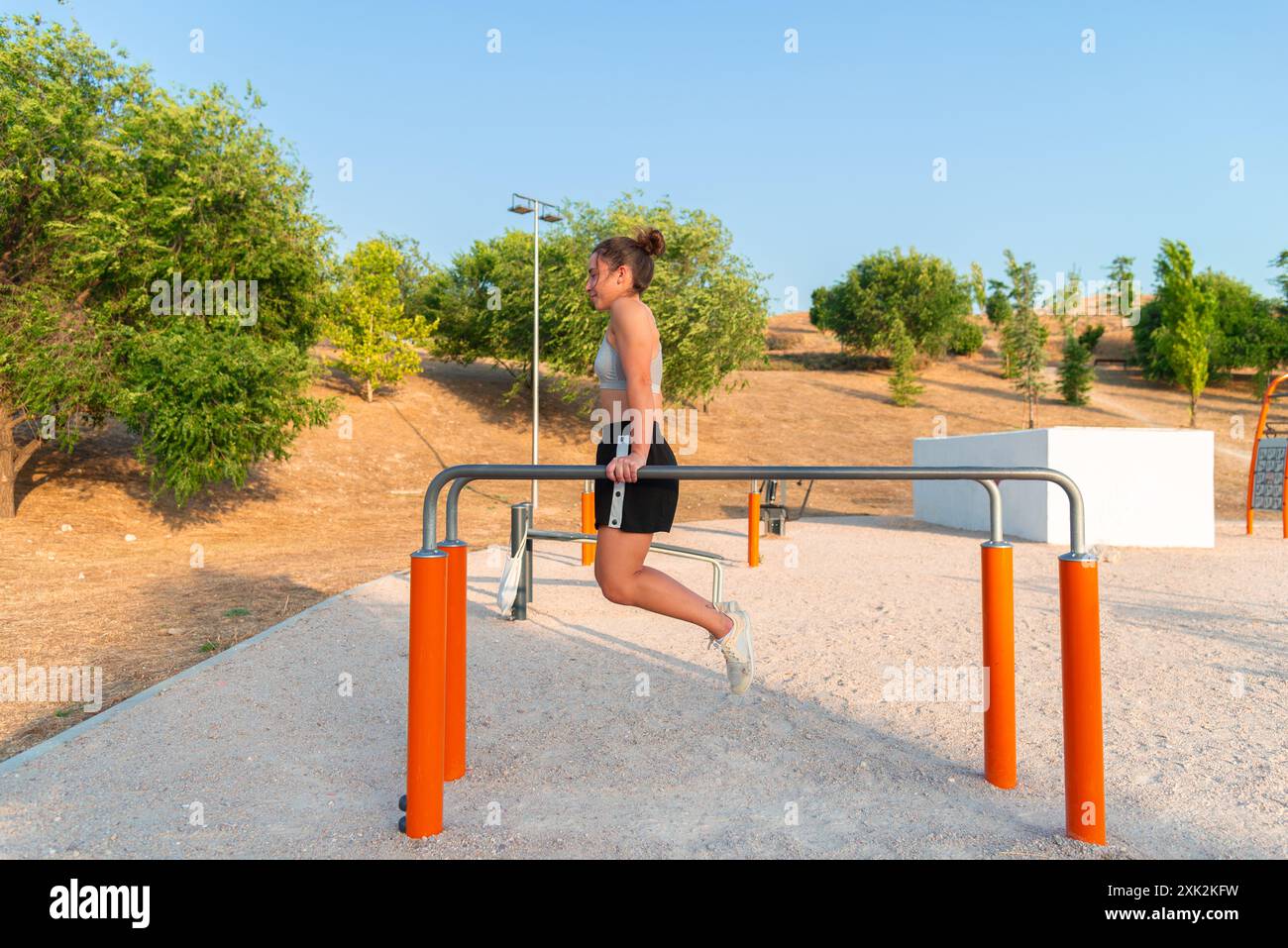 A young woman in athletic wear exercises on parallel bars in an outdoor ...