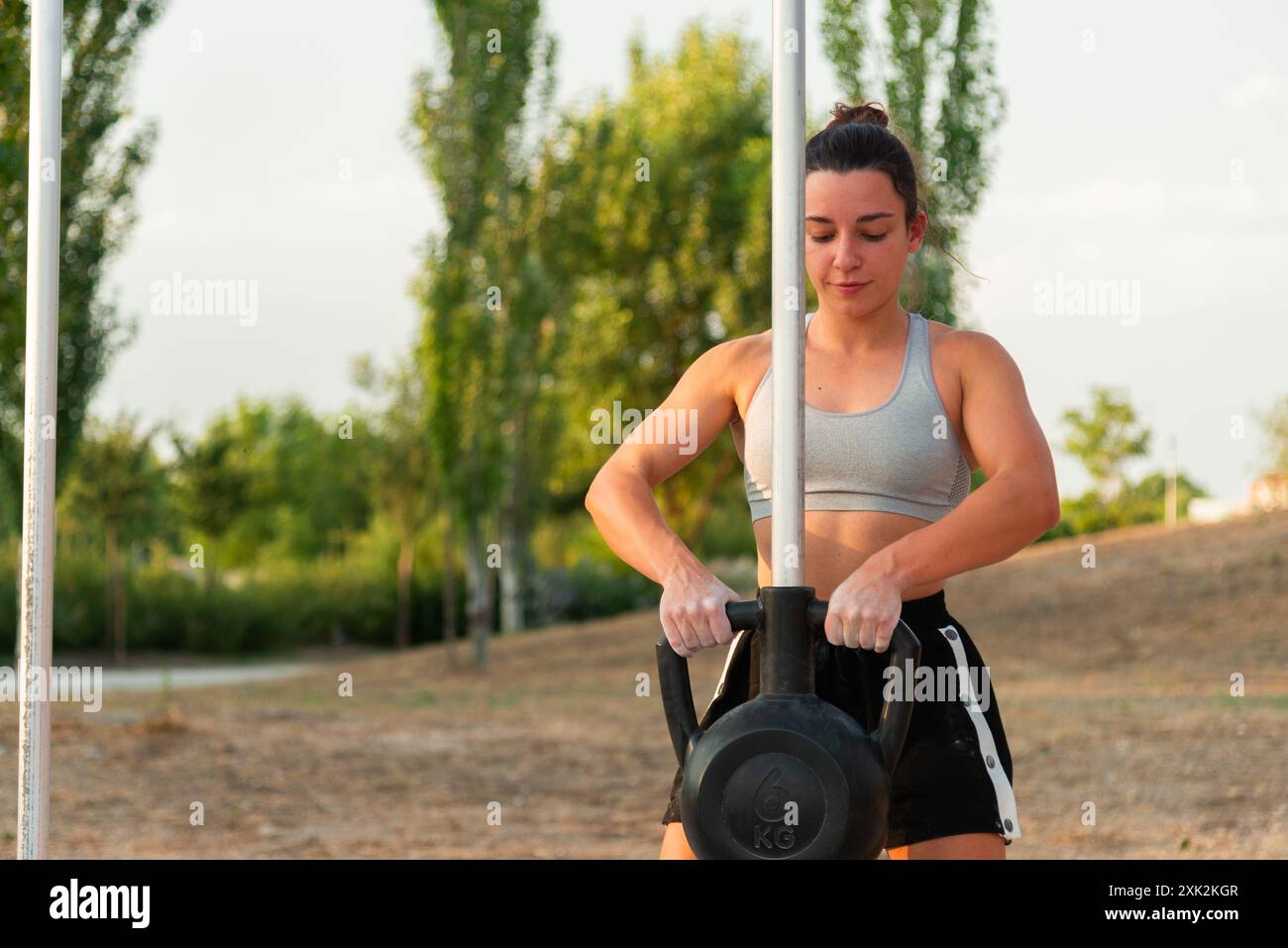 A focused young woman exercises by lifting weights at a local street ...