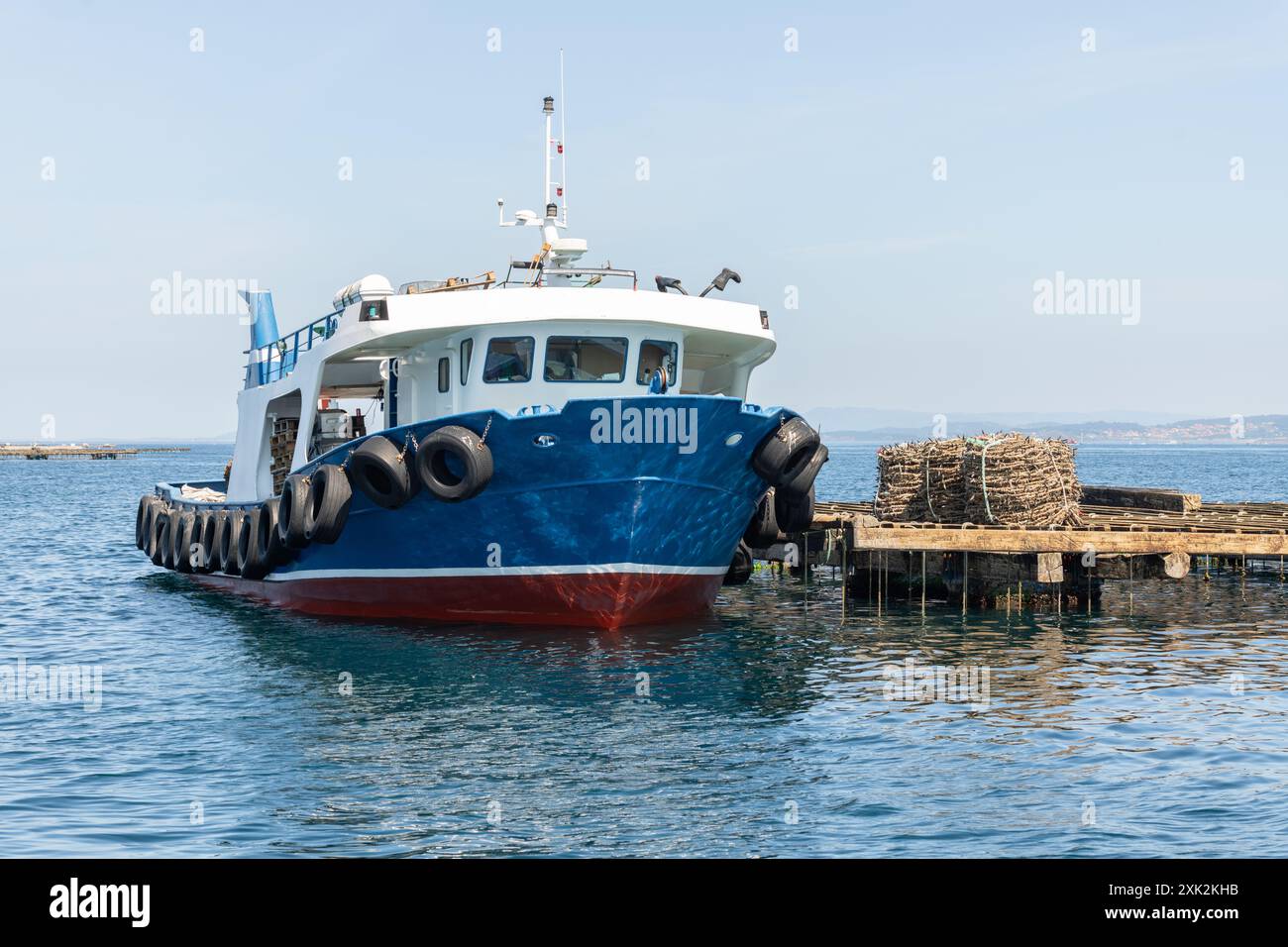A blue boat equipped to harvest mussels near a wooden platform, with ...