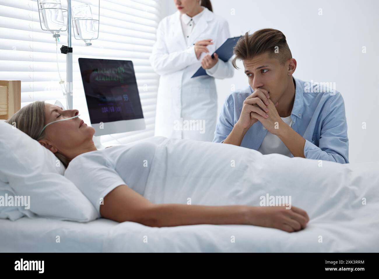 Coma patient. Sad young man near his unconscious mother in hospital ...