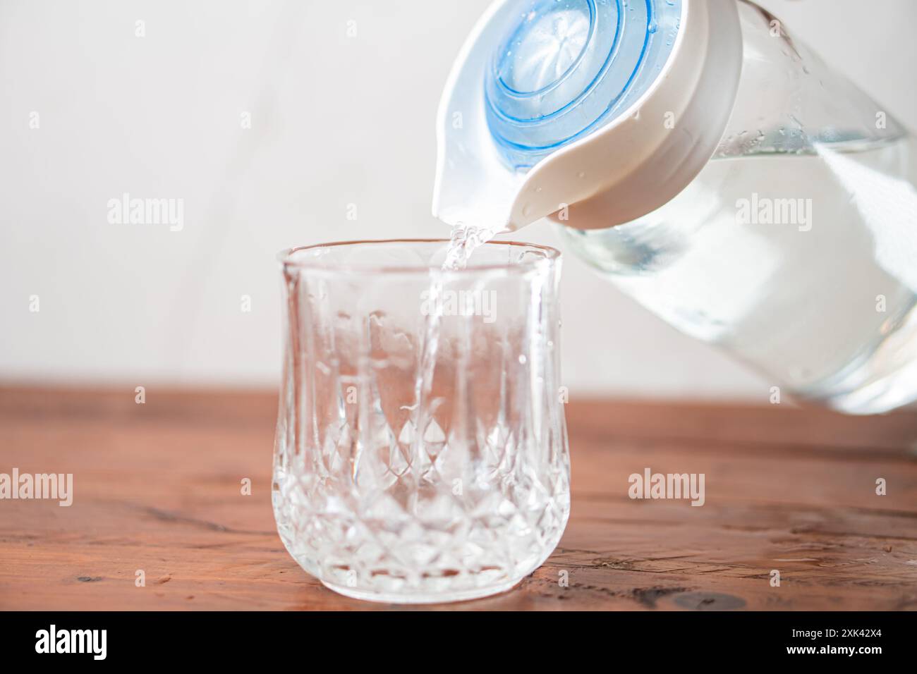 A clear glass being filled with water from a pitcher. The pitcher has a ...