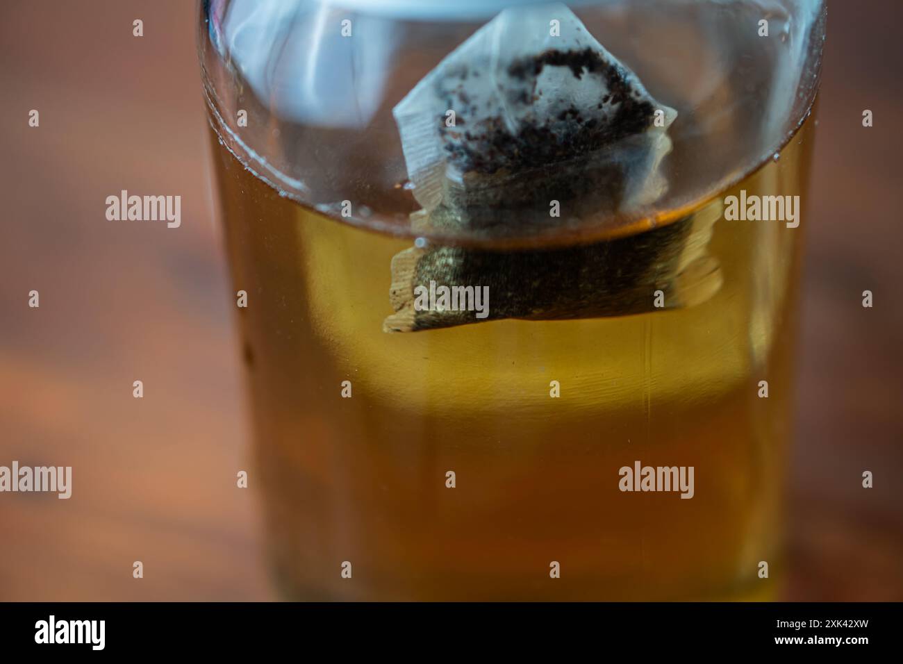 A close-up of a tea bag steeping in a glass jar filled with brewed tea ...