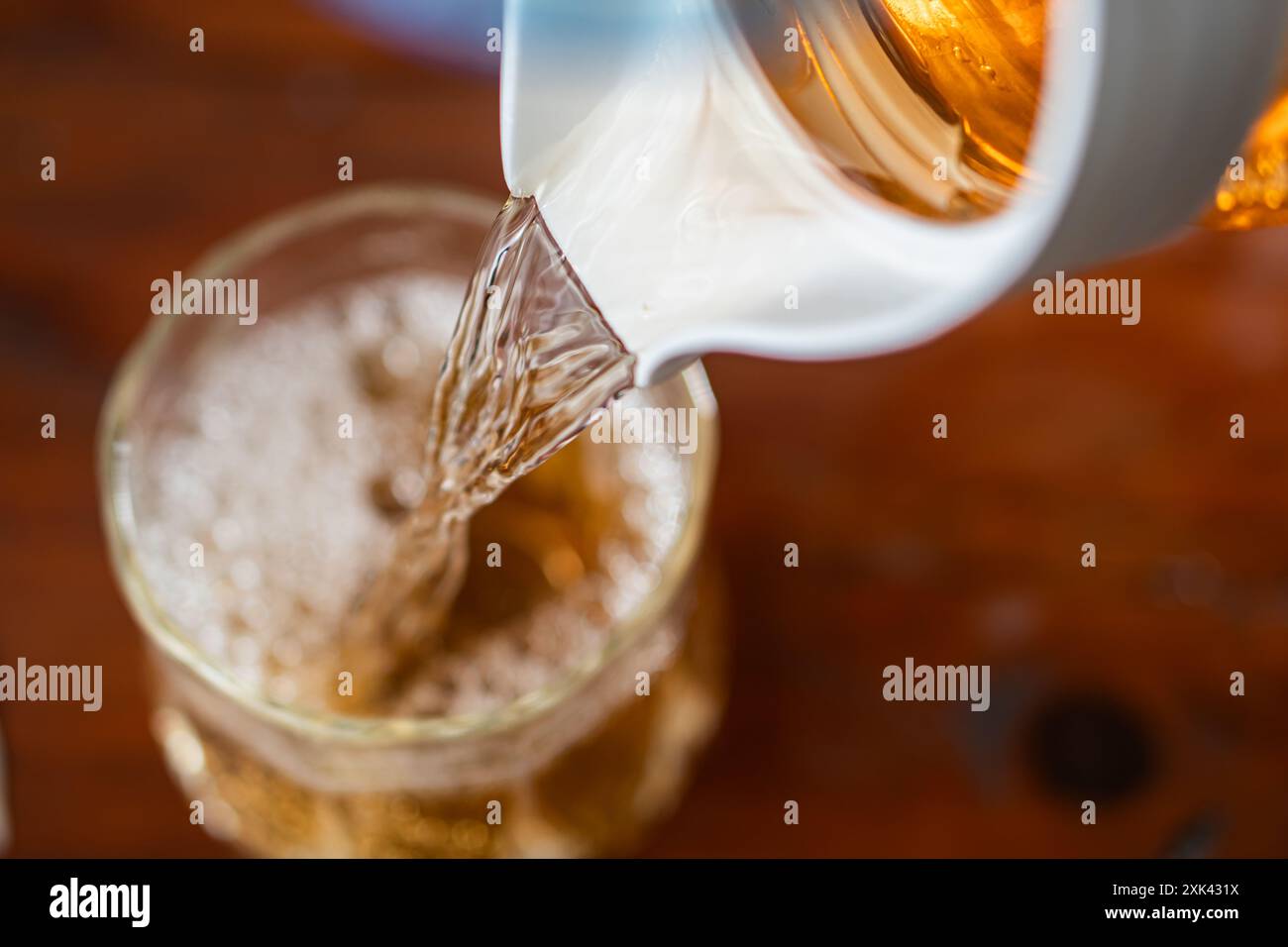 A close-up shot of a beverage being poured from a white pitcher into a ...