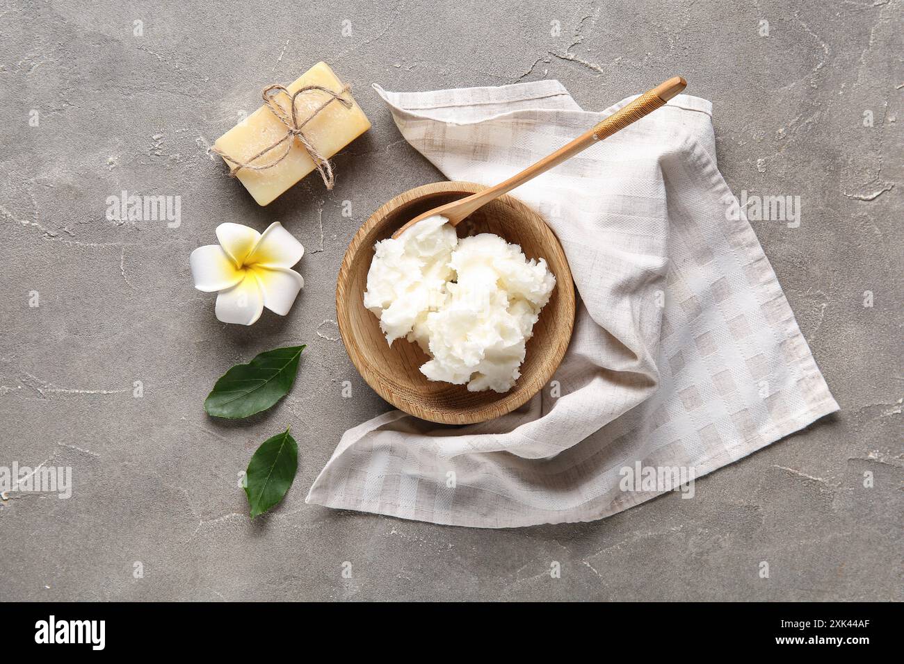 Bowl of shea butter with soap bar and plumeria flower on grey ...