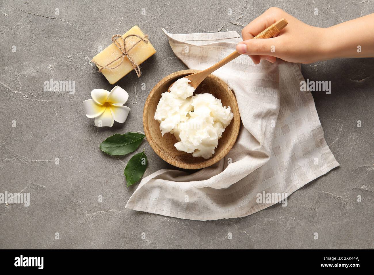 Female hand with spoon and bowl of shea butter, soap bar and plumeria ...