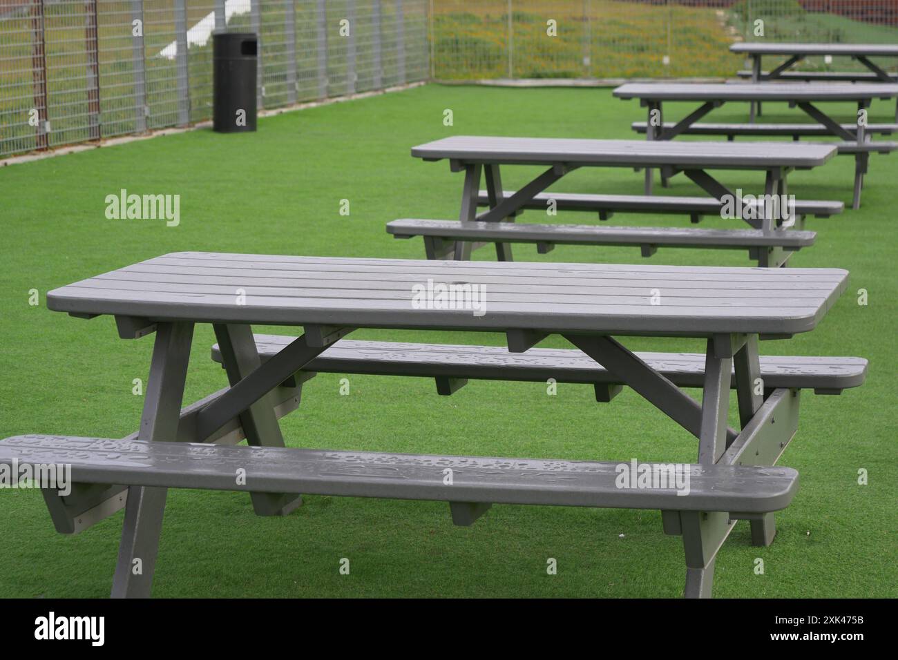 The parks artificial grass area features empty picnic tables under the ...