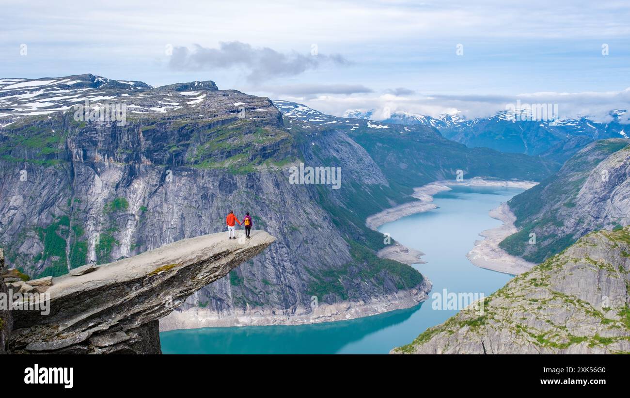 Two hikers stand on the edge of Trolltunga, Norway, a massive cliff ...