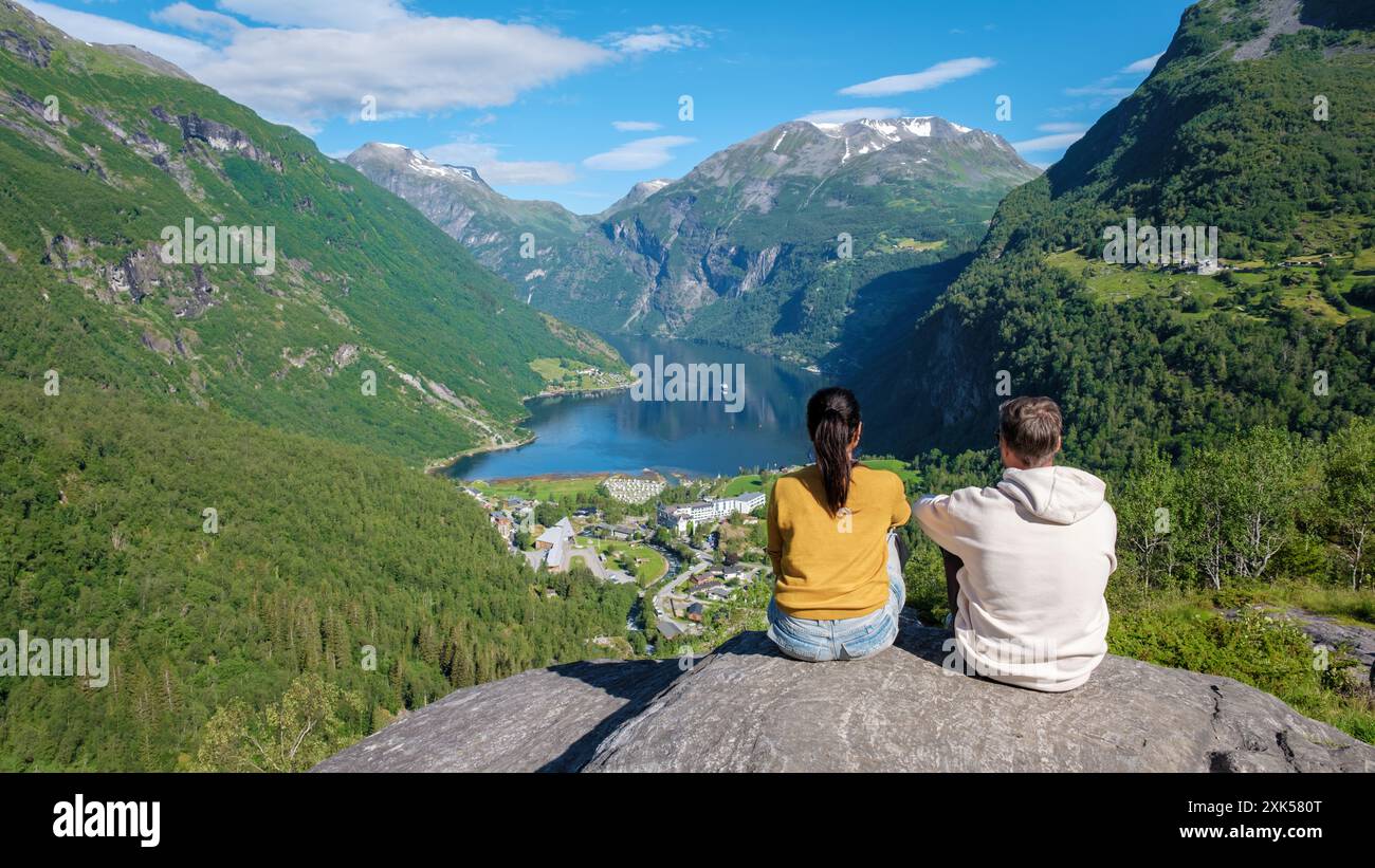 Two people sit on a rocky ledge overlooking a stunning Norwegian fjord ...