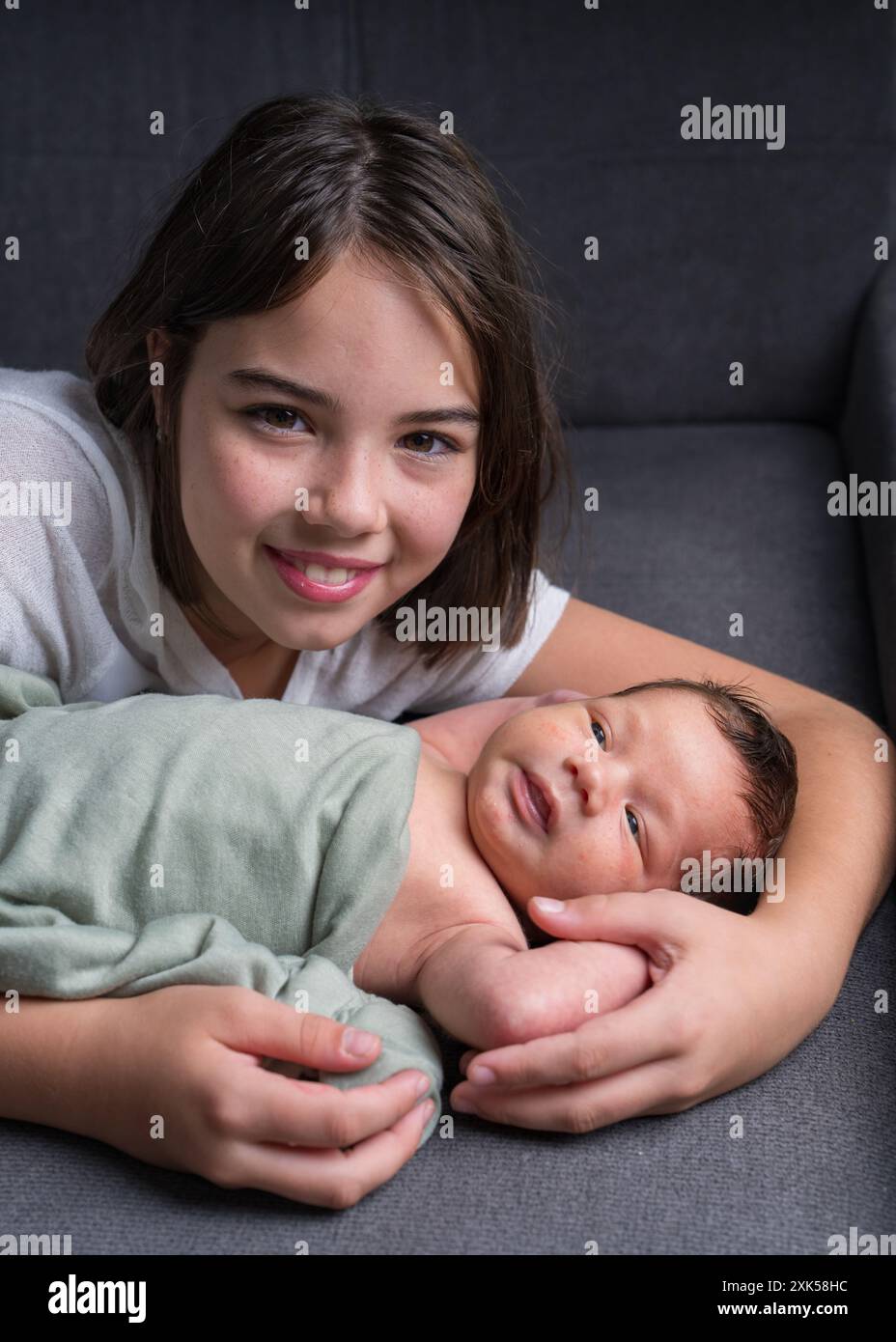 An older sister and her newborn little brother are lying on the sofa ...