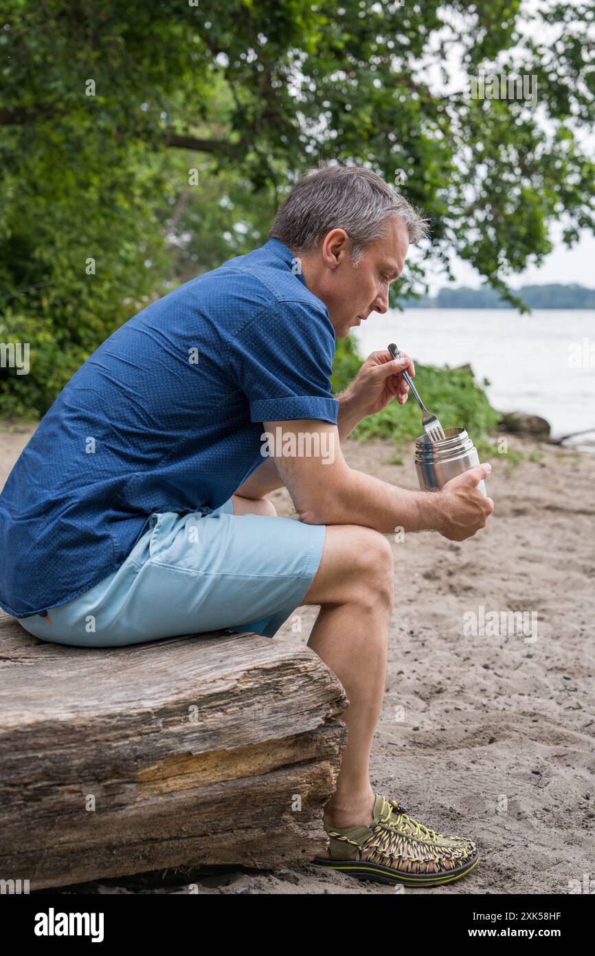 A middle-aged man travels, sits on the shore of the lake, eats food ...